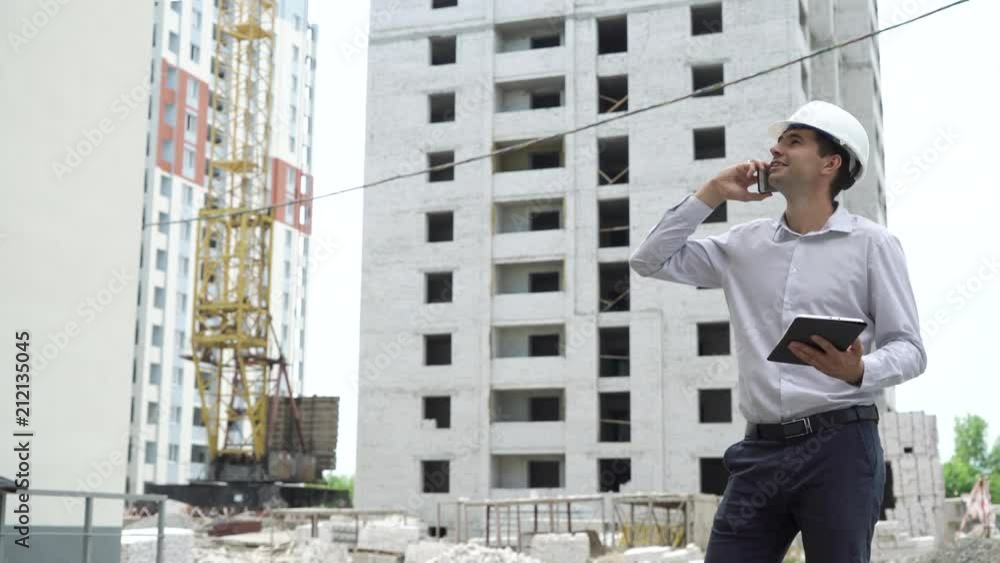 Construction site engineer with tablet talking on mobile phone checking ...