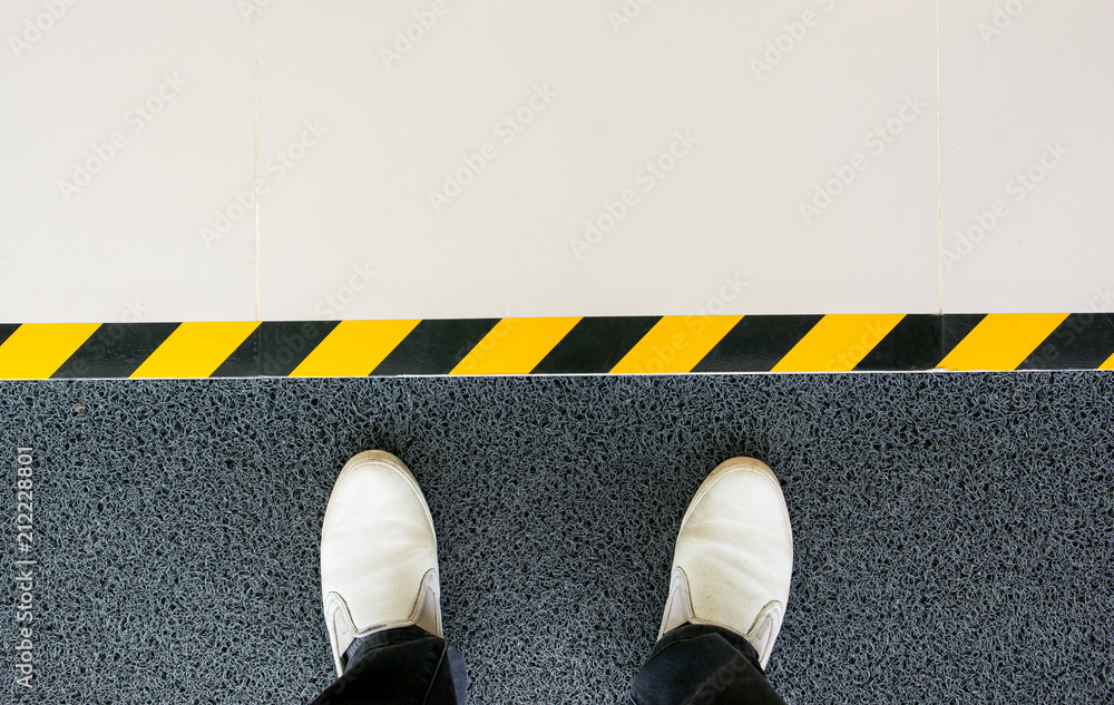 Mind your step line on the floor with men feet standing at entrance ...