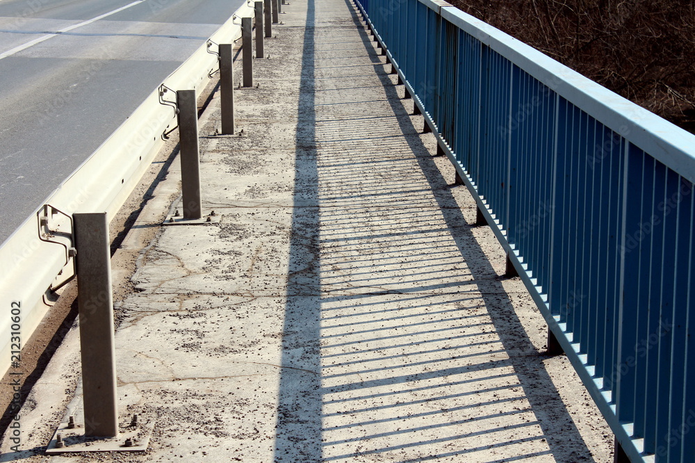 Bridge sidewalk with sand on cracked asphalt between guardrail on left ...