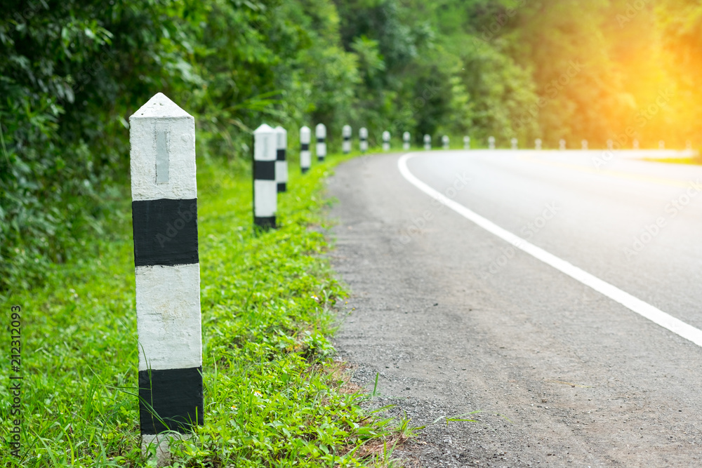 Black and white milestones with green grass roadside, Trees roadside in ...