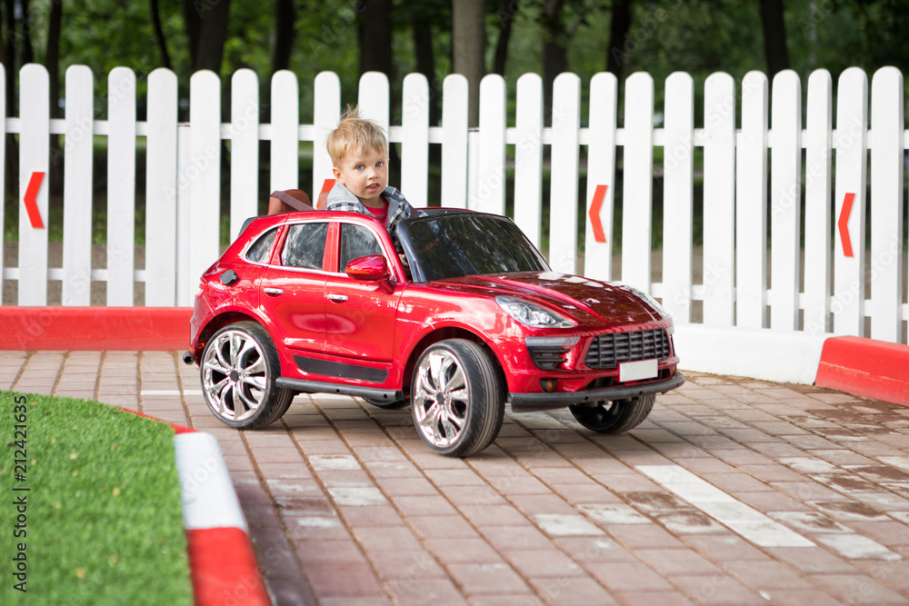 Little smiling boy is driving a car on kid's go-karting. Three year-old ...