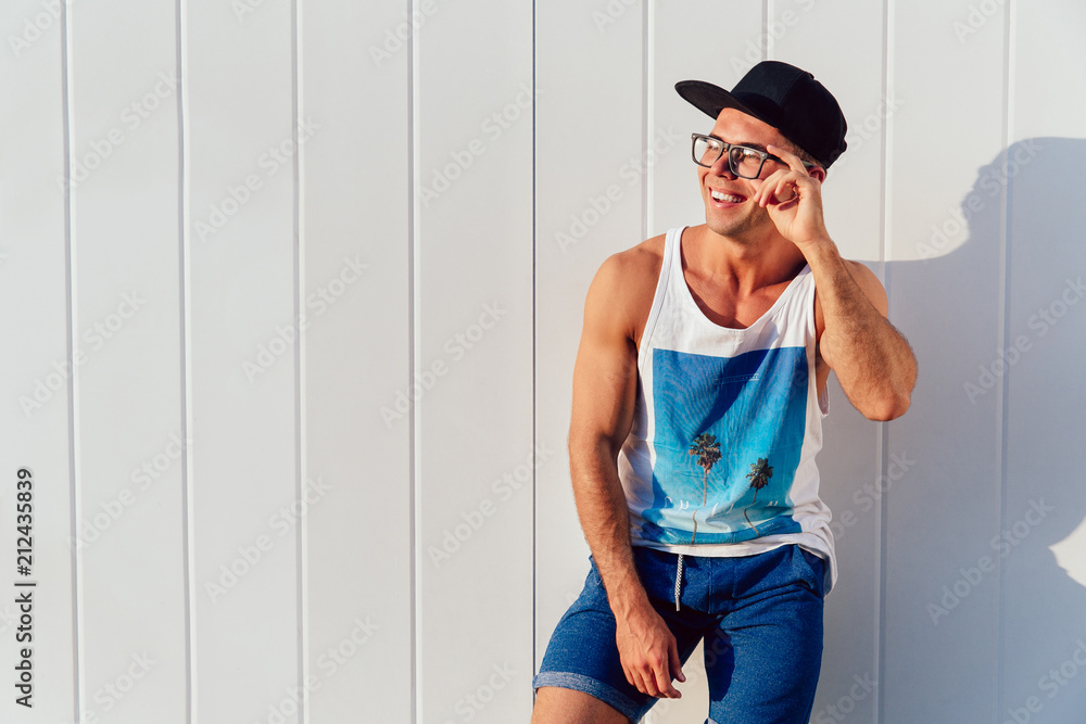 Outdoor photo of attractive young man in rap cap, keeping his hand on ...