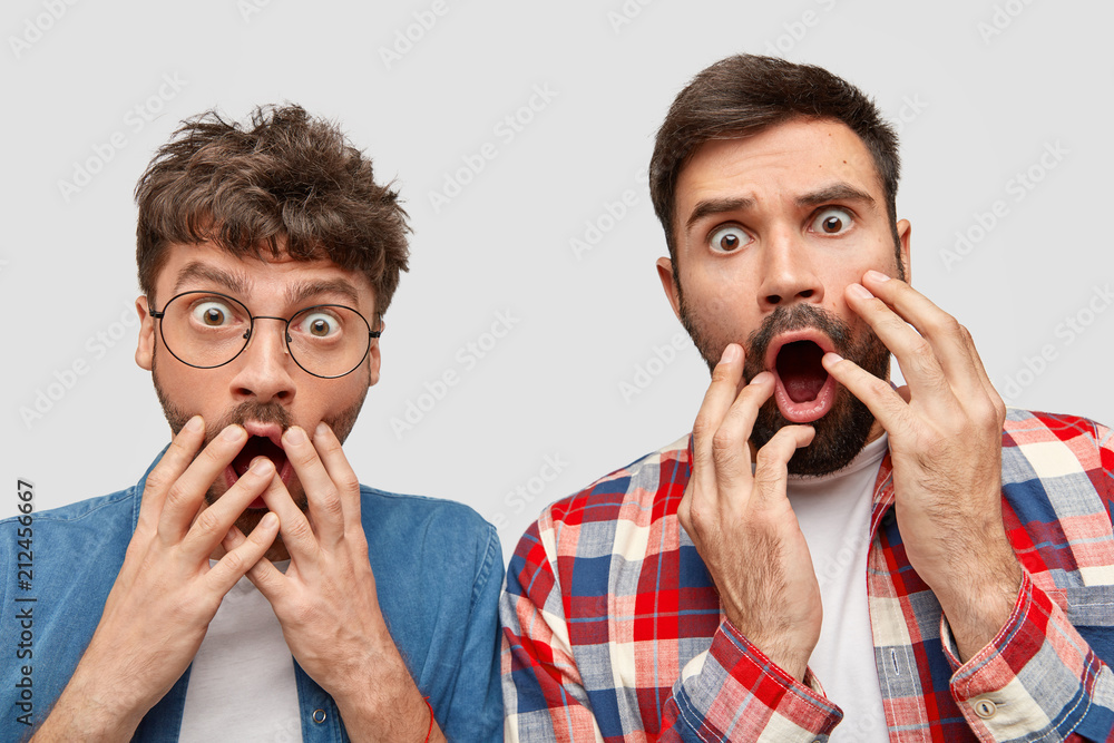 Two amazed bearded young guys stare at camera with frightened nervous ...