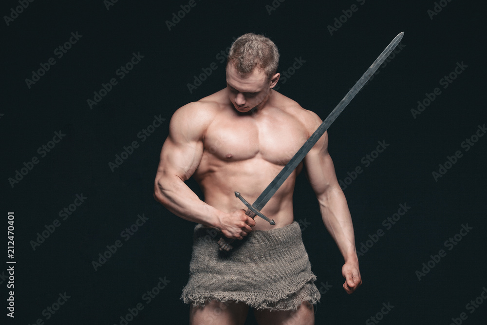 Bodybuilder man posing with a sword isolated on black background ...