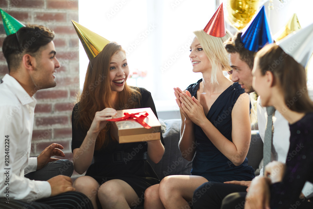 Surprised girl with gift-box saying thanks to her friends while going ...