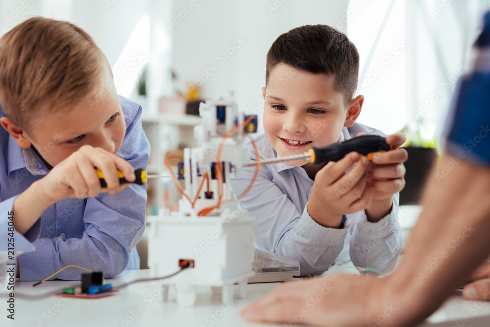 Modern science. Positive delighted boys building a robot while having a ...