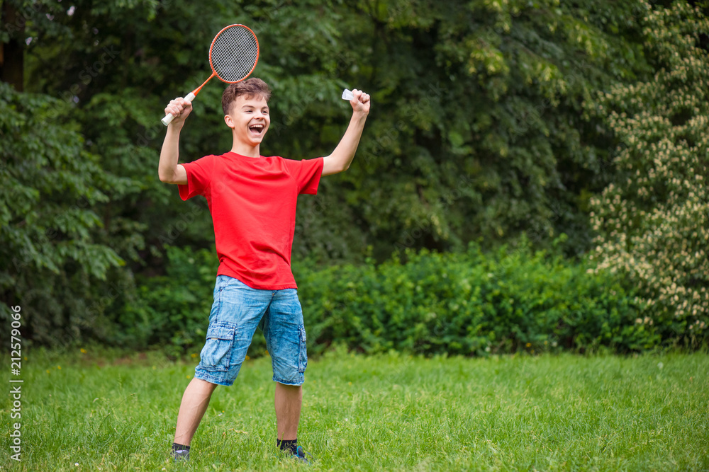 Young teen boy playing badminton in meadow with forest in background ...