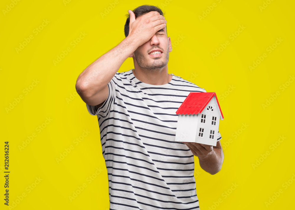 Handsome real estate agent holding a house stressed with hand on head ...