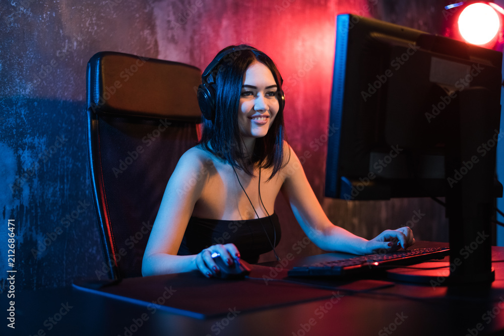 A cute female gamer girl sits in a cozy room behind a computer and ...