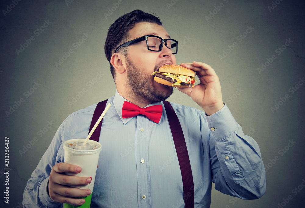 Overweight business man eating with appetite a burger holding a can of ...