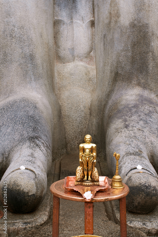 Brass statue infront of a gigiantic monolithic statue of Bahubali, also ...