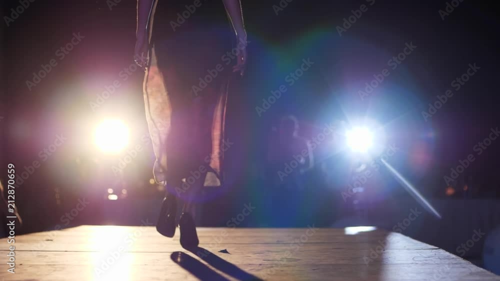 Catwalk model into high heels into dresses goes on podium in lighting ...