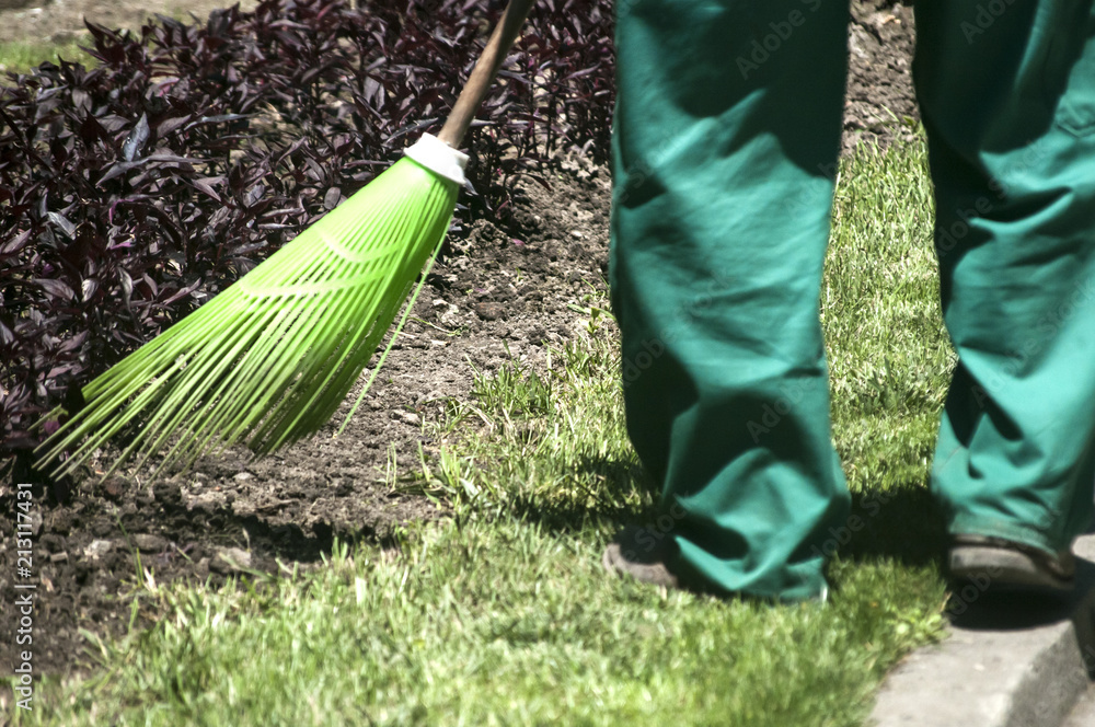 Maintenance worker in park garden cleans the flower beds with plastic ...