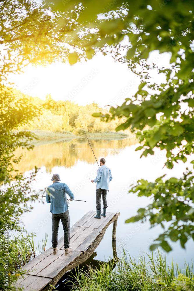 Two male friends fishing together standing on the wooden pier during ...