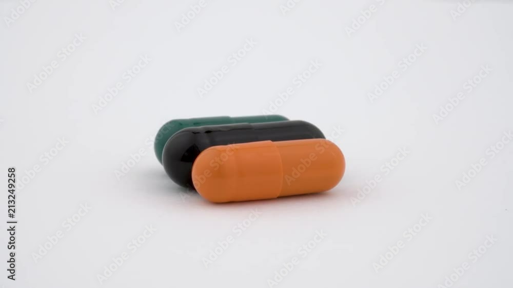 Three hard starch capsules rotating on the turn table. Orange, black ...
