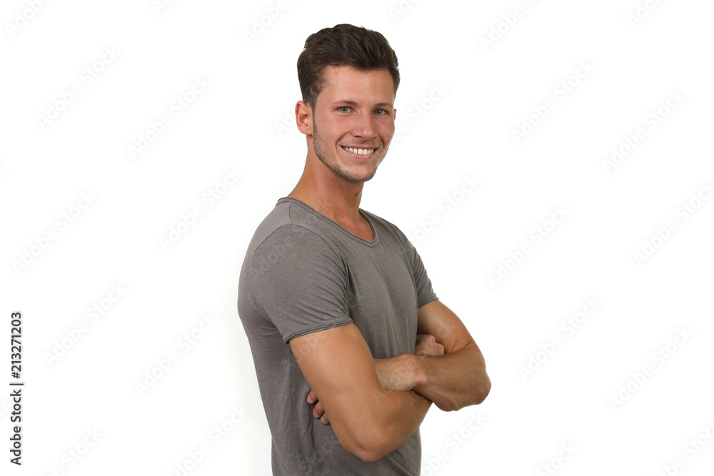 Junger Mann steht lachend und mit verschränkten Armen vro weißem ...