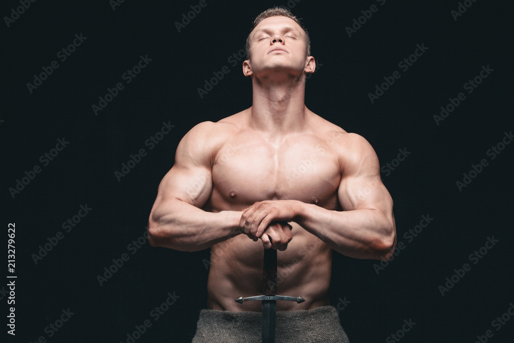 Bodybuilder man posing with a sword isolated on black background ...