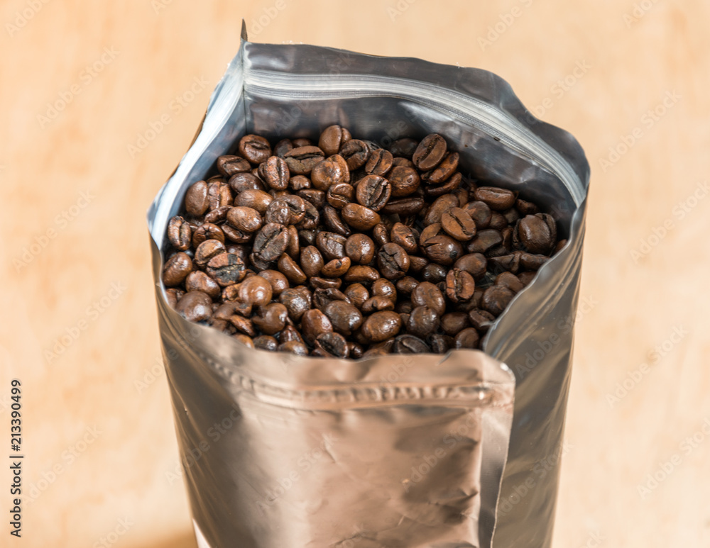 Coffee beans in a plastic foil package on wooden background. Roasted ...