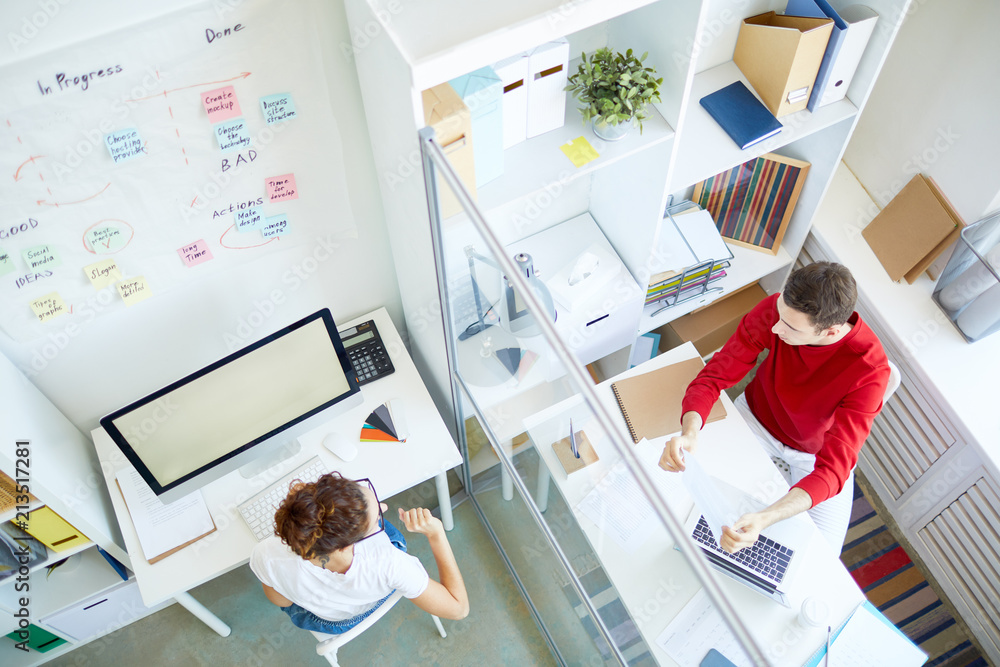 Overview of two office workers sitting by their workplaces and talking ...
