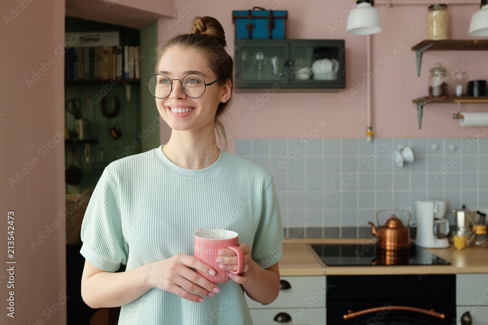 Closeup picture of young optimistic European Caucasian female spending afternoon on her kitchen ...