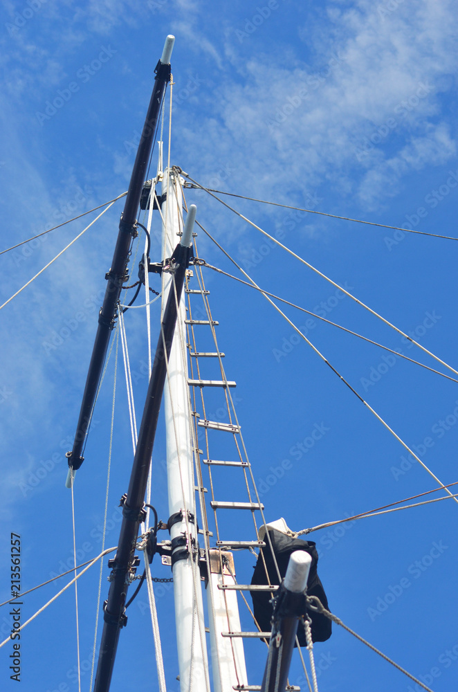 The mast of yacht rising against a blue sky. A ladder and rope rigging ...
