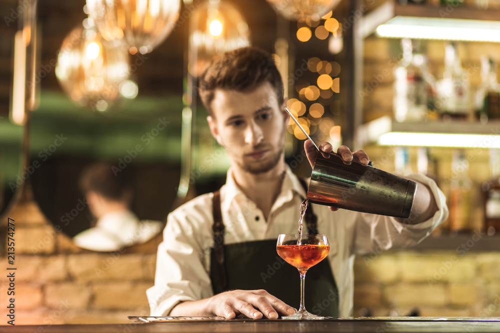 Perfect skills. Pleasant young barman standing behind a bar counter ...