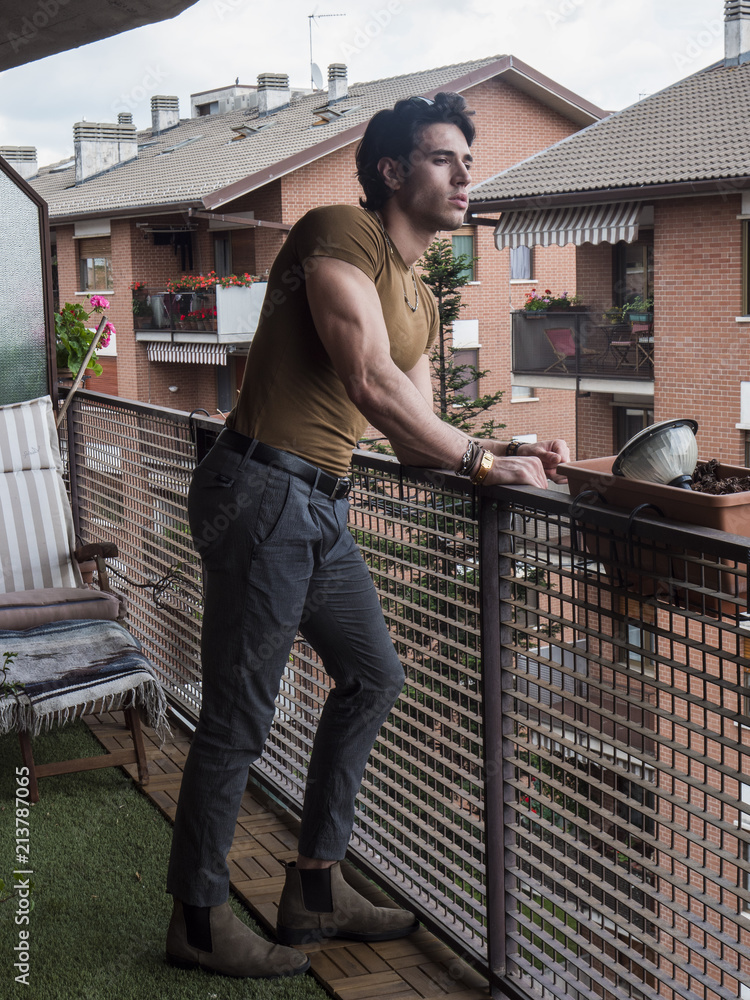 Handsome dark haired young man standing in a balcony, looking out and ...