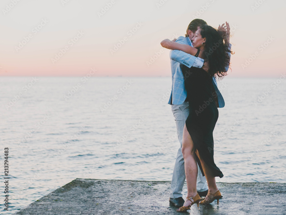 Portrait of young attractive couple dancing latin bachata near sea. Dance performed by a ...
