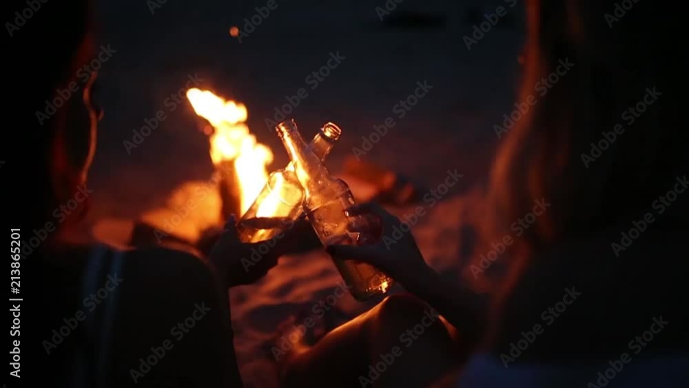 Beach party at sunset with bonfire. Friends sitting around the bonfire ...