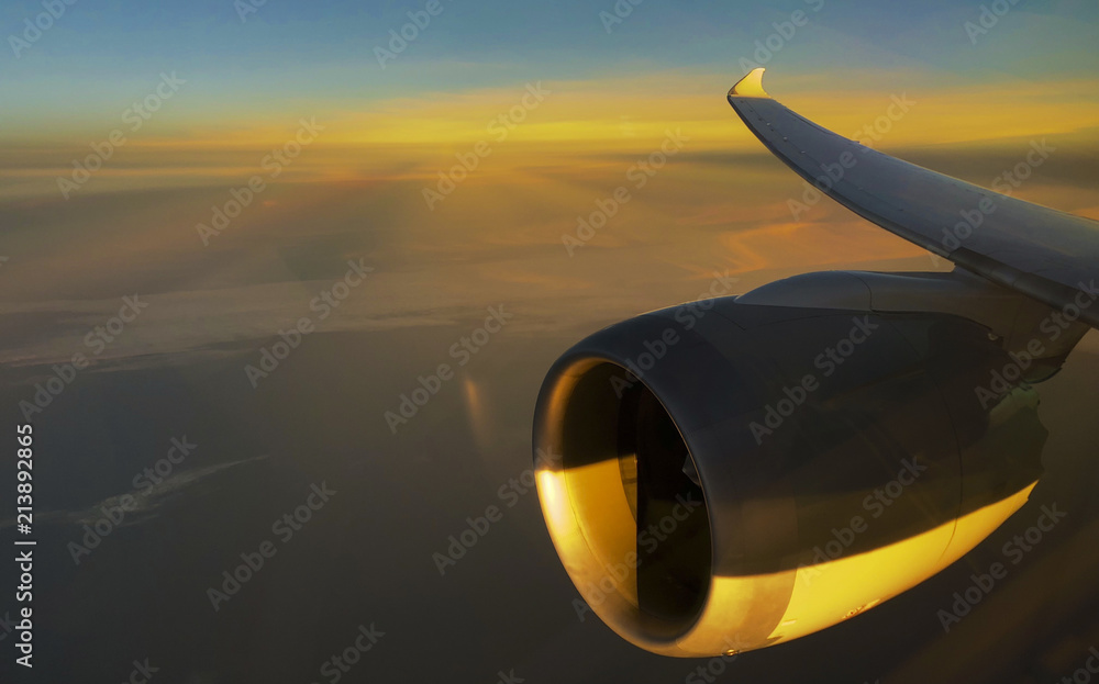 Through window view of plane engine and wing against rising sunrays ...