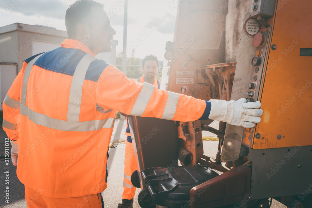 Two refuse collection workers loading garbage into waste truck emptying ...