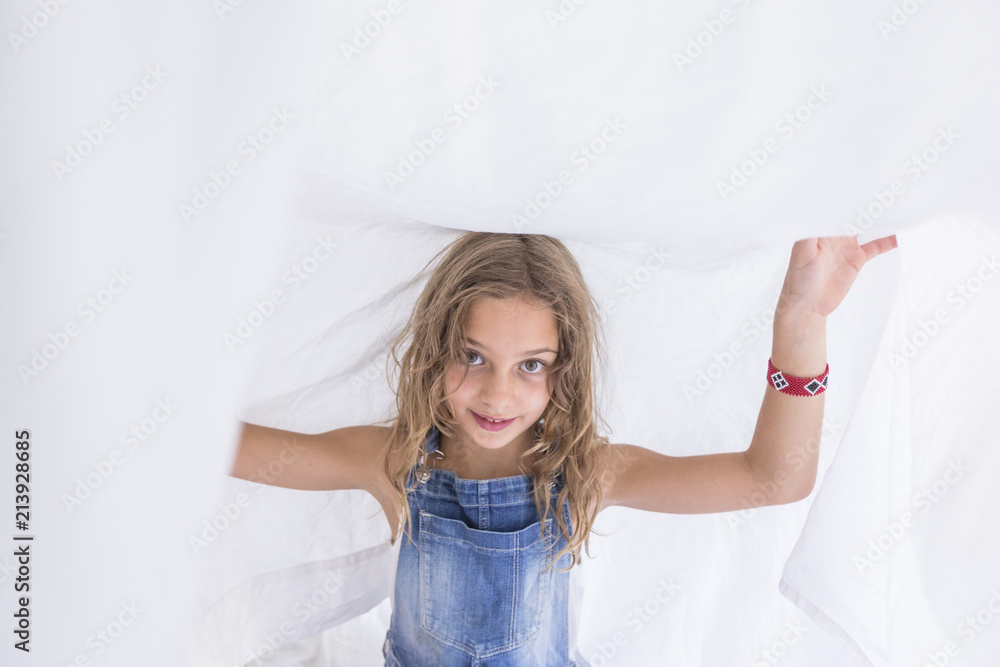 beautiful kid girl playing under white sheets on bed. Fun indoors ...