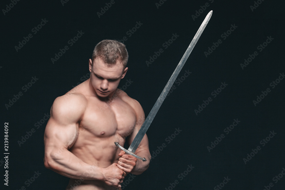 Bodybuilder man posing with a sword isolated on black background ...