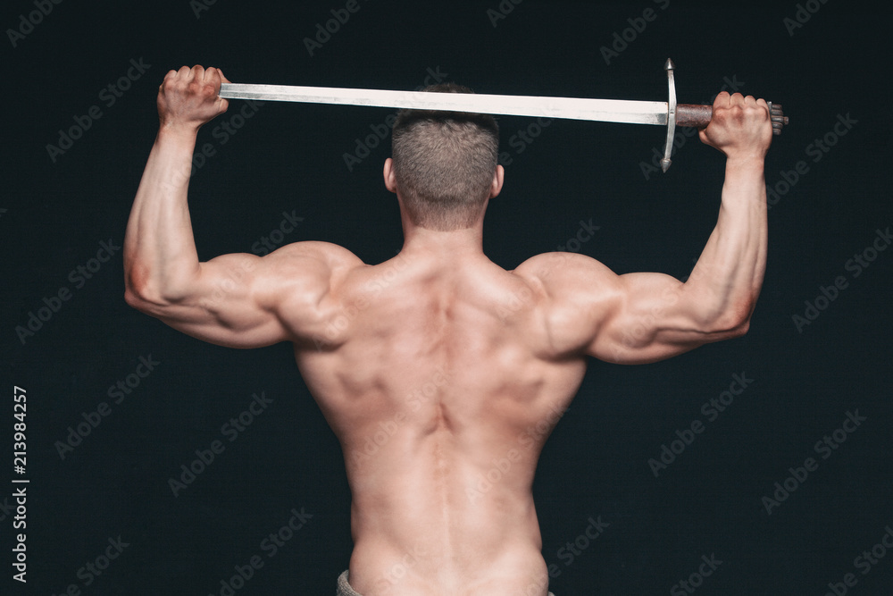 Bodybuilder man posing with a sword isolated on black background ...