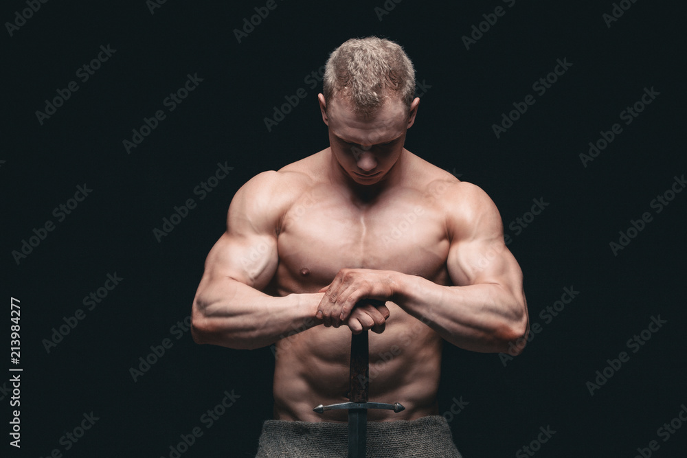 Bodybuilder man posing with a sword isolated on black background ...