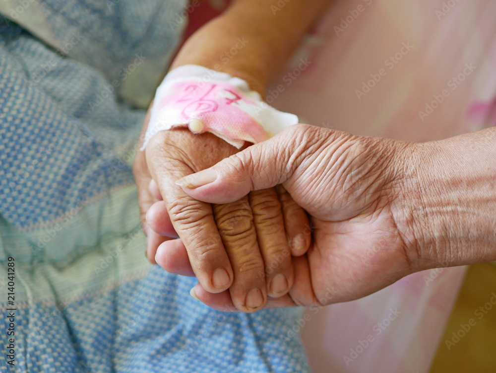 A hand of an old man holding a hand of a sick old lady with intravenous ...