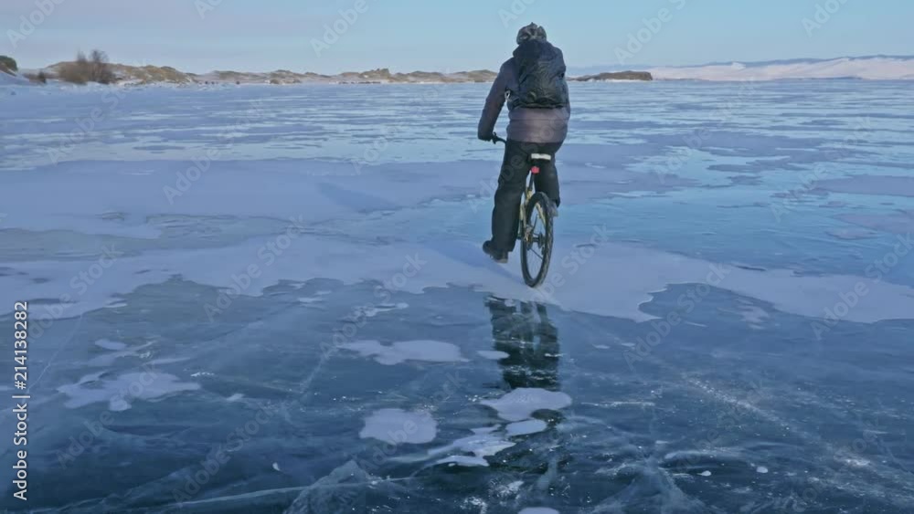 Man is riding a bicycle on ice. The cyclist is dressed in a gray down ...