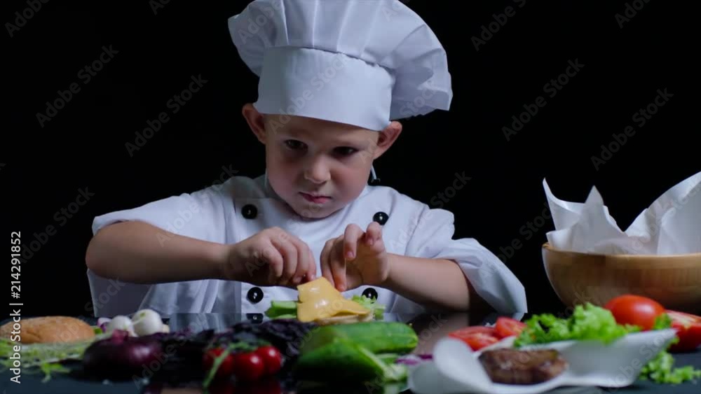 Time lapse of cheerful boy cooking a burger. He wears chefs suit and ...