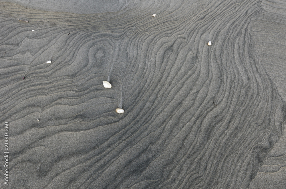 Tide patterns on the surface of a grey, sandy beach in the South Island ...
