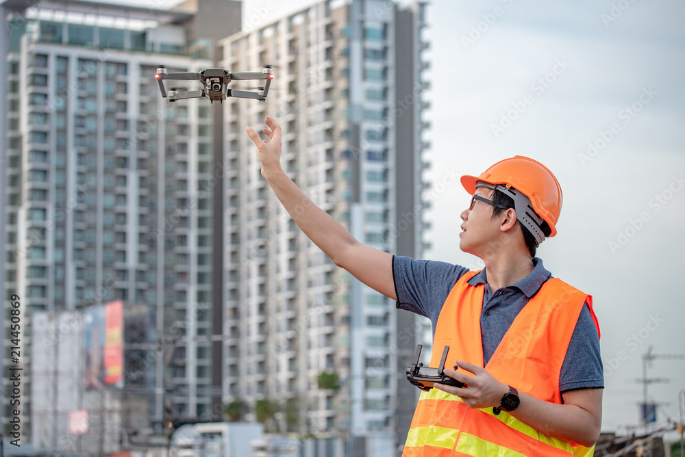 Young Asian engineer man flying drone over construction site. Using ...
