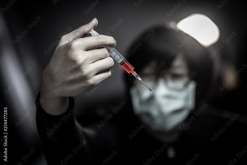 Young man in the mask using syringe for red drug injection. Drug abuse ...