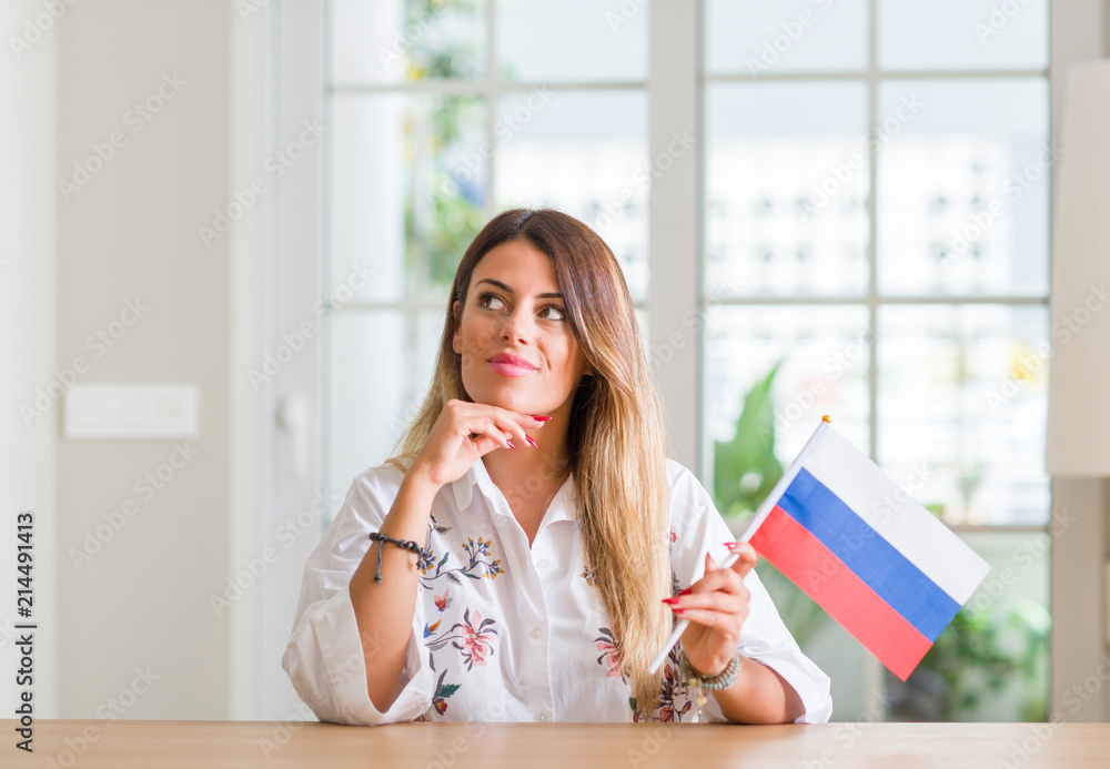 Young woman at home holding flag of Russia serious face thinking about ...