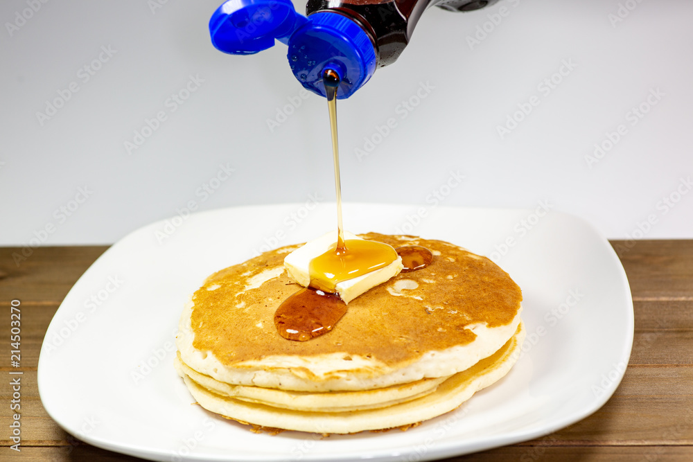 Pouring syrup from a blue tip bottle onto the square of butter on a ...
