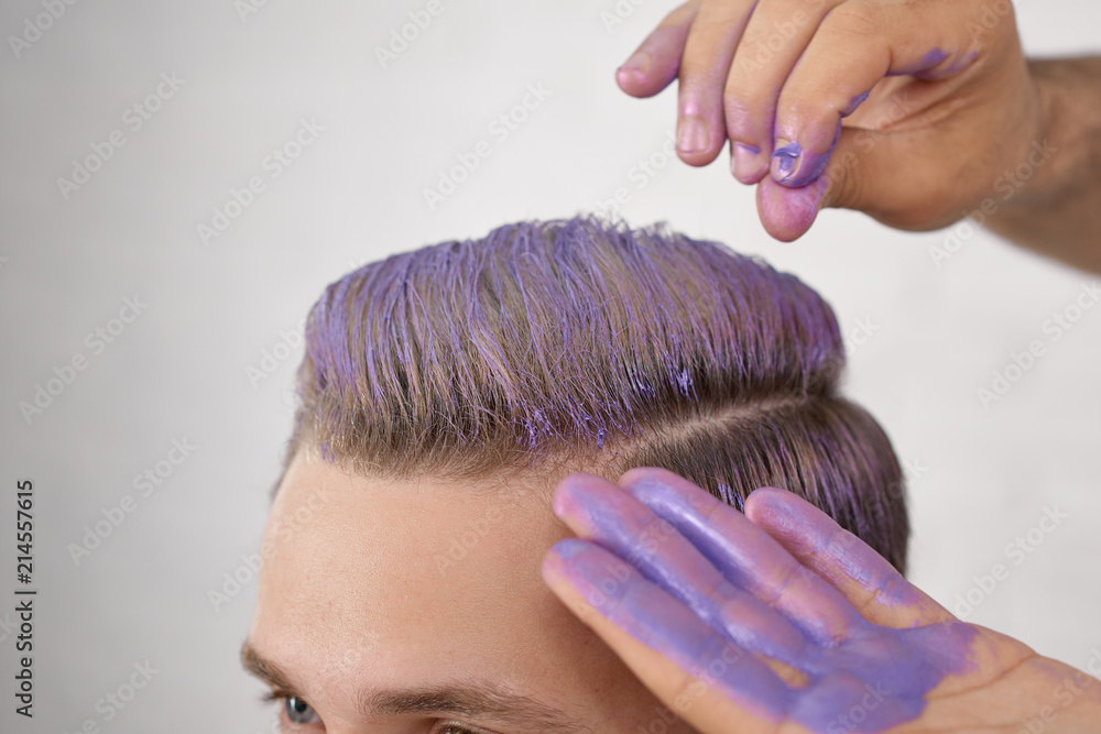Barber's hand toning young client's hair in violer color. Hands are ...