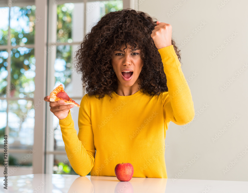 African american woman choosing between apple and pizza slice annoyed ...