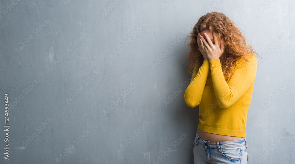 Young redhead woman over grey grunge wall with sad expression covering ...