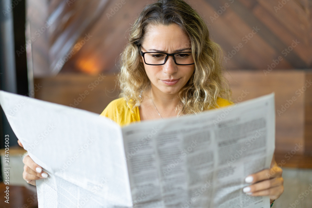 Frowning young woman reading job ads in newspaper. Displeased girl ...