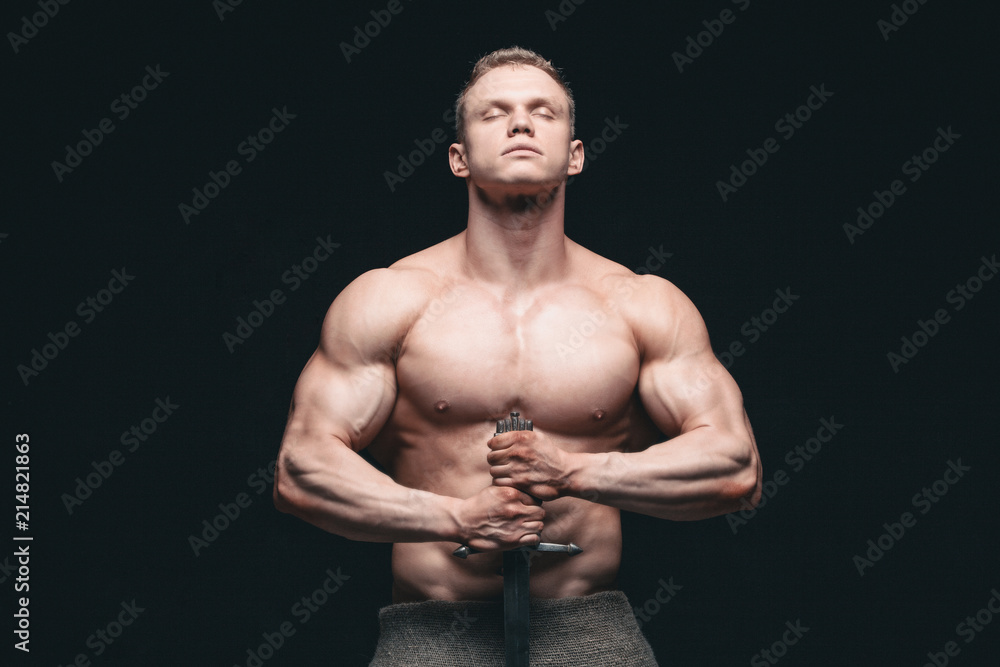 Bodybuilder man posing with a sword isolated on black background ...