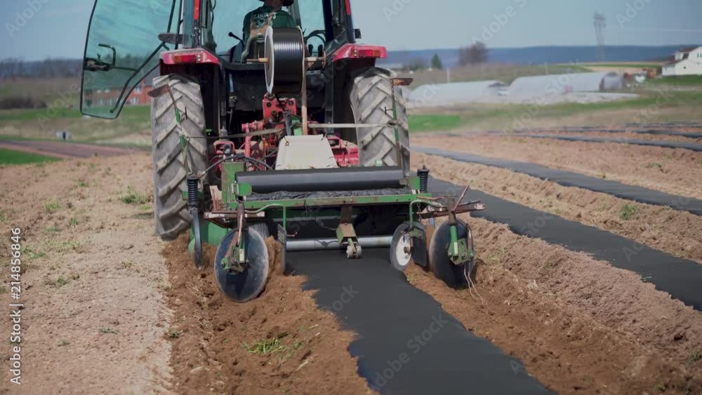 Closeup of plastic mulching equipment laying down plastic mulch behind ...