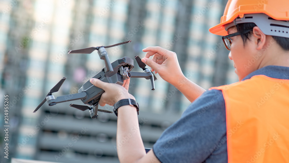 Young Asian engineer holding drone at construction site. Using unmanned ...
